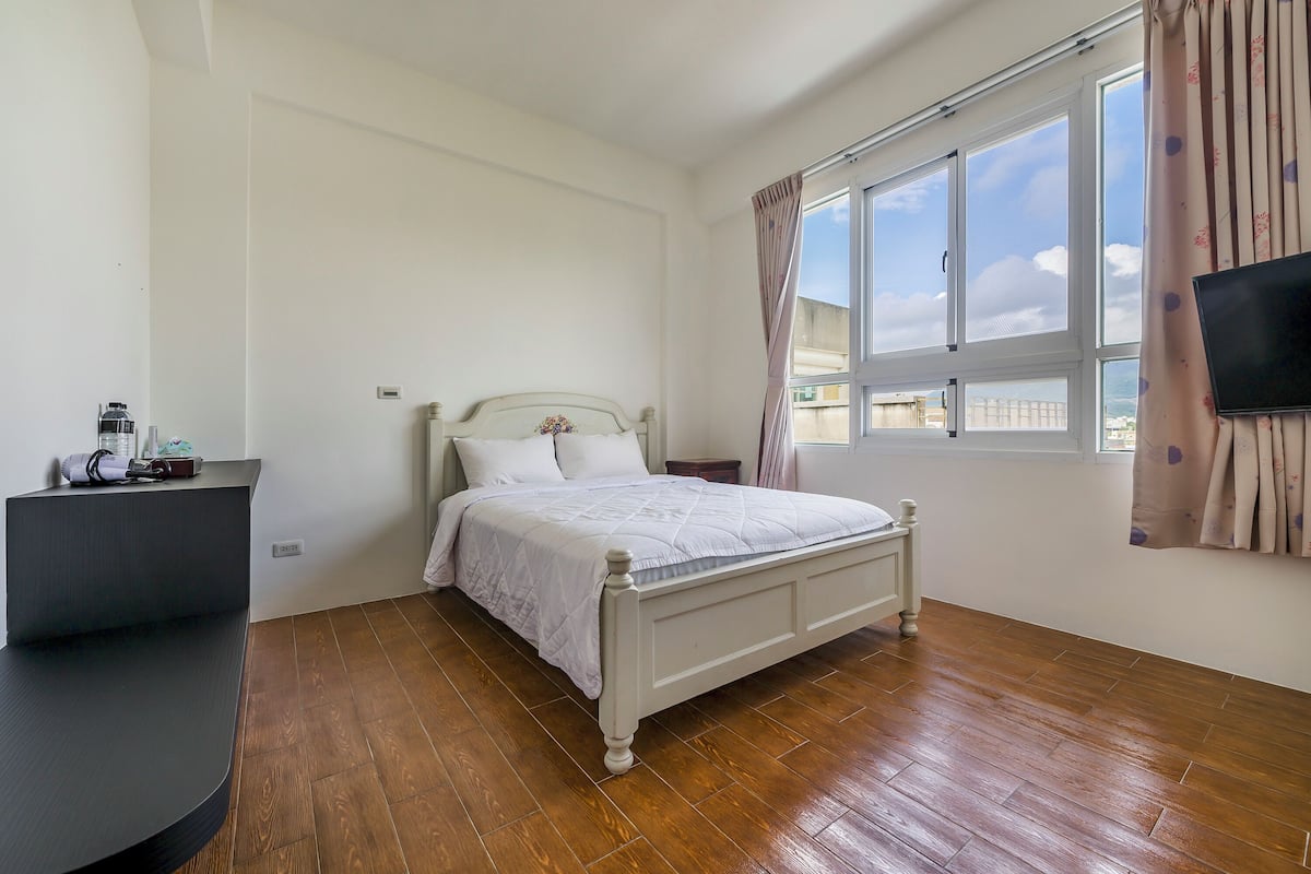 Quarto com cama, escrivaninha e televisão.