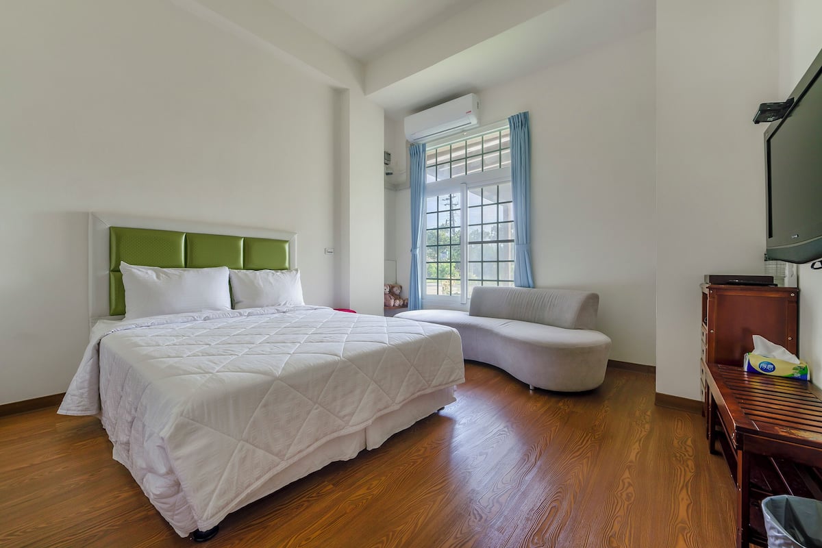 Quarto de hotel com cama, sofá, escrivaninha de madeira e televisão.