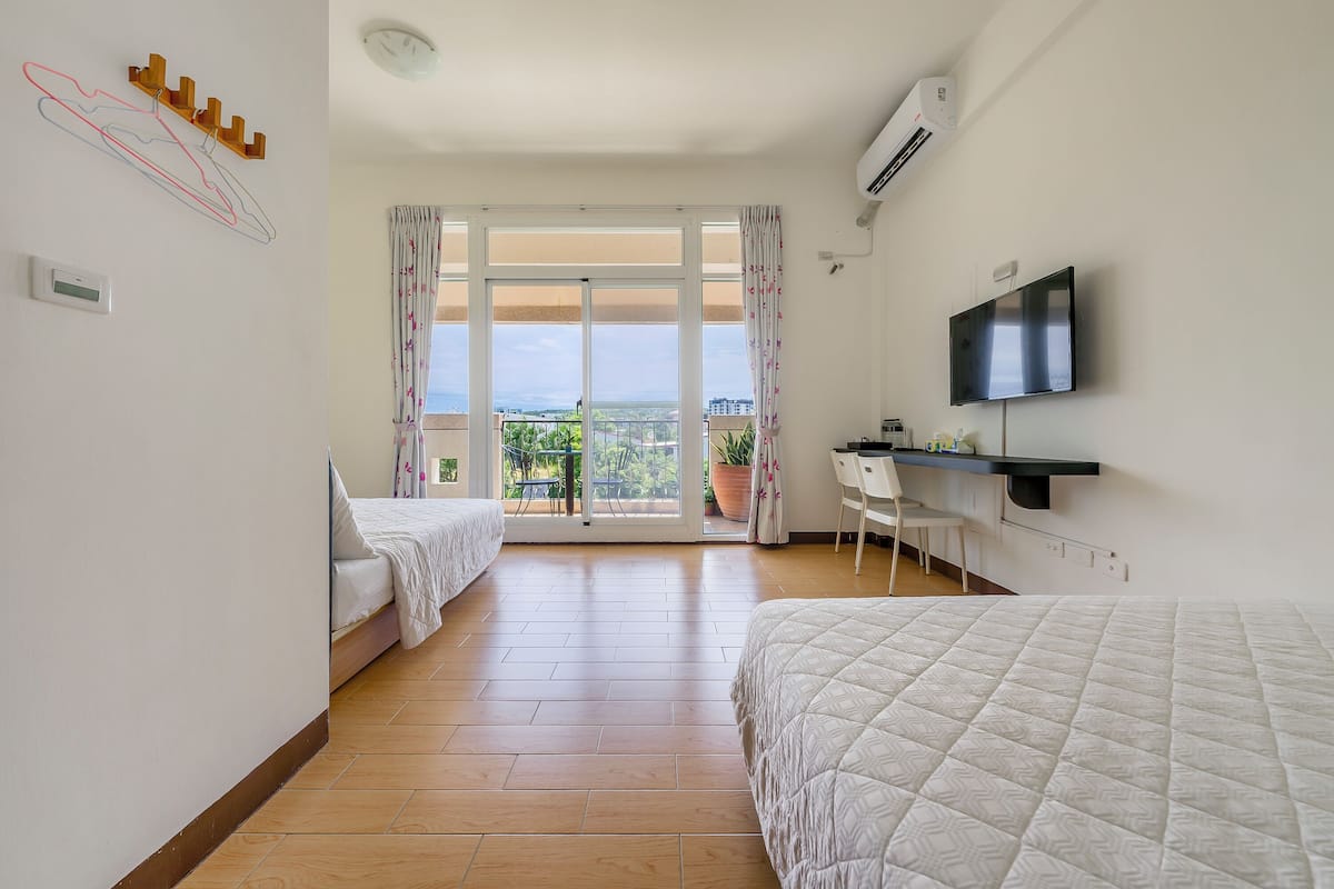 Quarto de hotel com duas camas, televisão, escrivaninha e varanda com vista.
