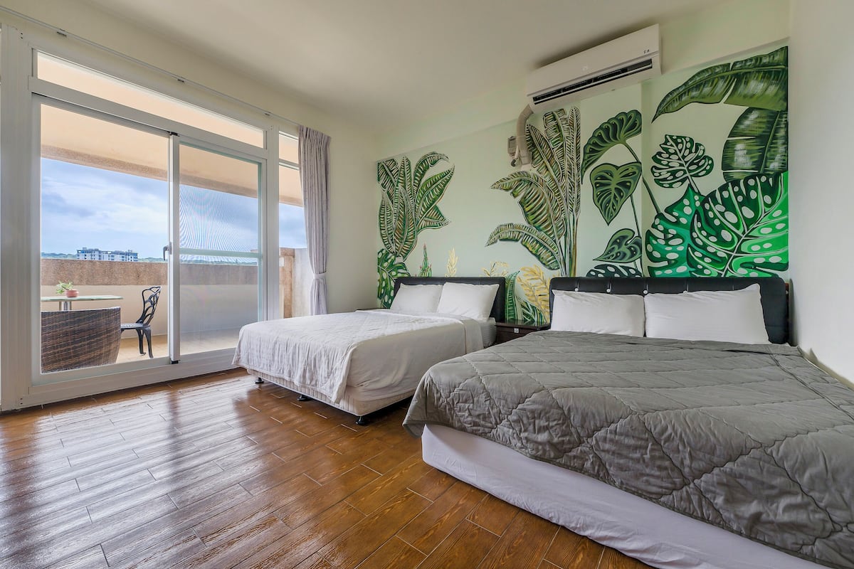 Quarto com duas camas, varanda e um grande mural na parede.