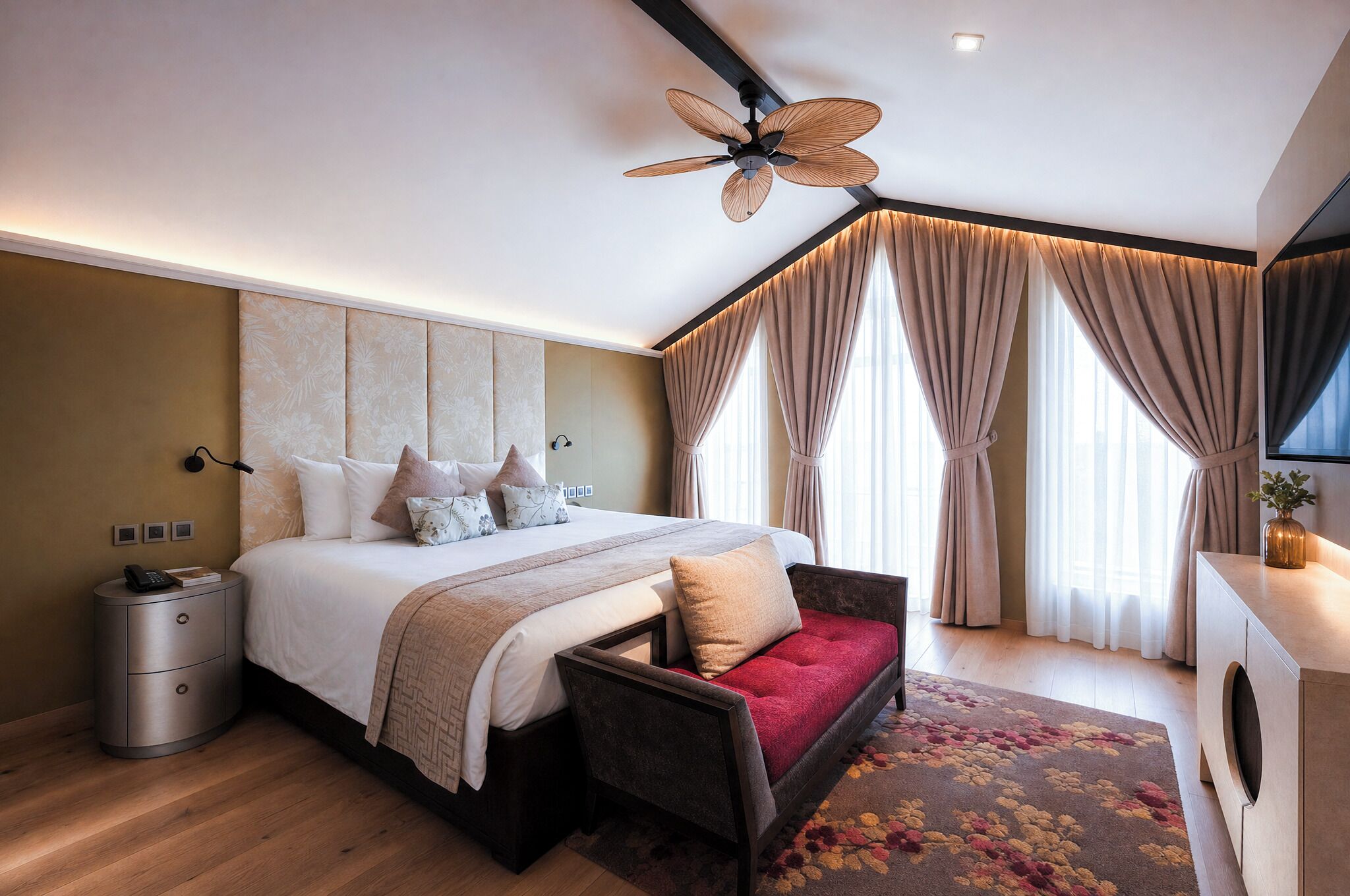 Quarto moderno com uma cama grande, mesa de cabeceira, ventoinha no teto e vista para o exterior por grandes janelas.
