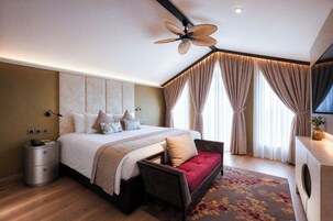 Quarto moderno com uma cama grande, mesa de cabeceira, ventoinha no teto e vista para o exterior por grandes janelas.