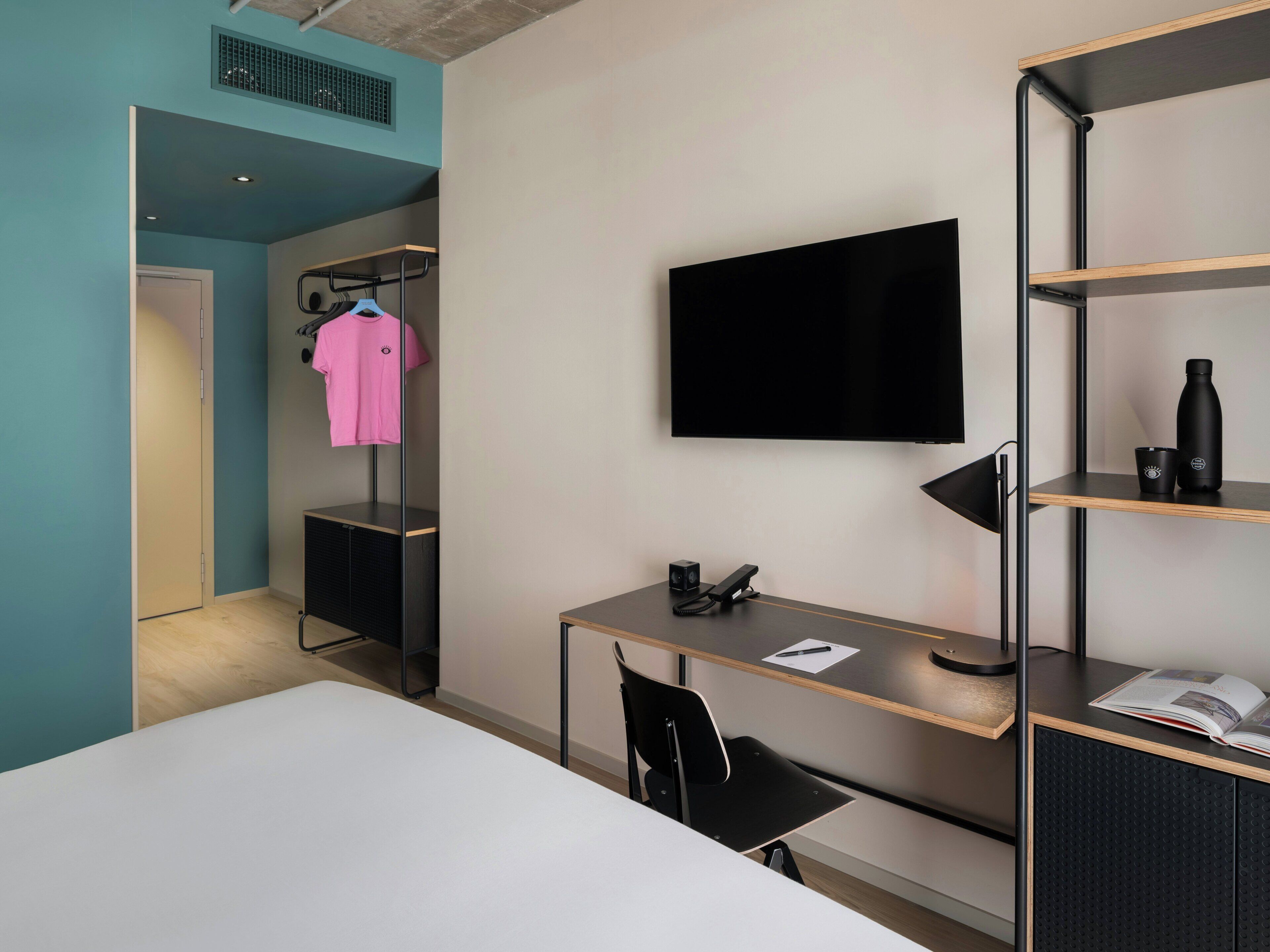 Quarto de hotel moderno com cama, escrivaninha, cadeira, televisão e guarda-roupa.