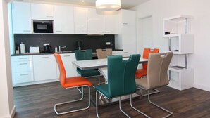 Cozinha moderna com armários brancos, micro-ondas preto e área de jantar com mesa e cadeiras brancas.