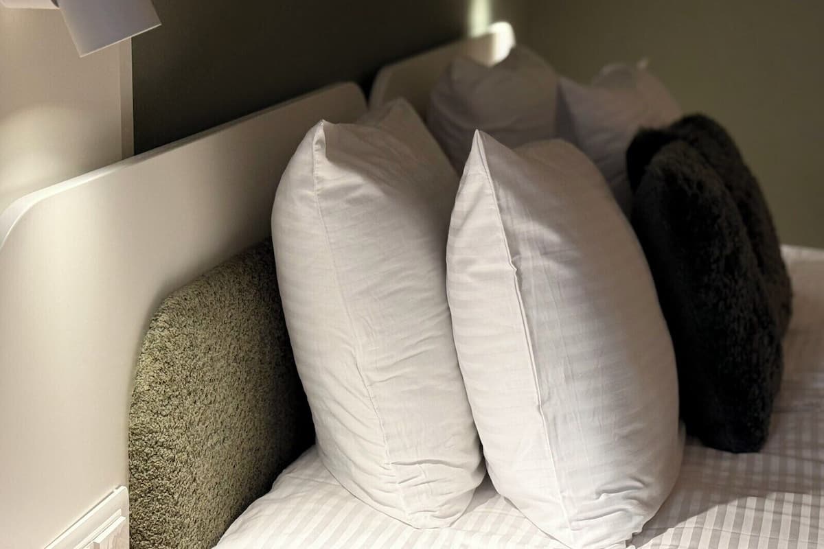 Uma cama com roupa de cama branca e listrada, um travesseiro verde texturizado e um travesseiro escuro texturizado.