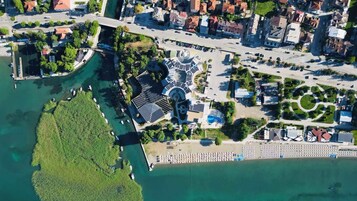 Vista aérea de uma área costeira com um porto de iates, um edifício grande com telhado circular e edifícios residenciais ao redor.