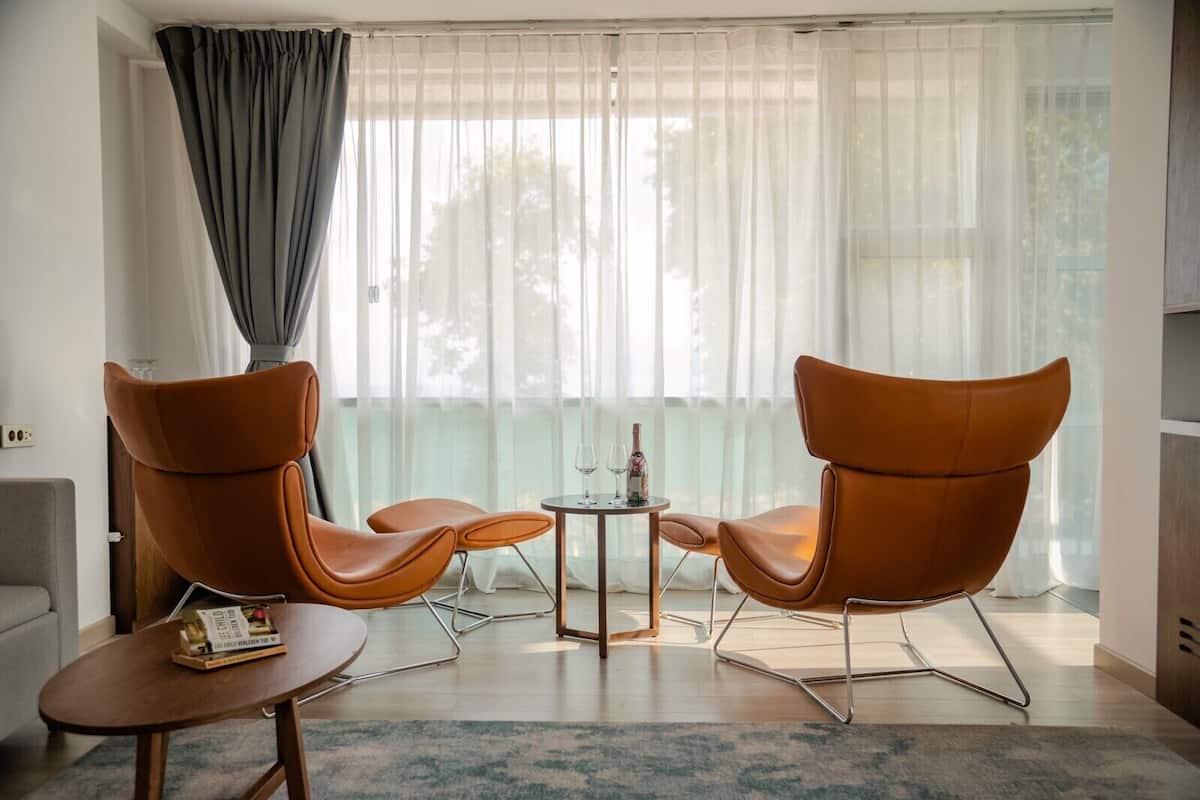 Uma sala de estar moderna com duas poltronas de couro, uma mesa redonda pequena e uma estante de livros.
