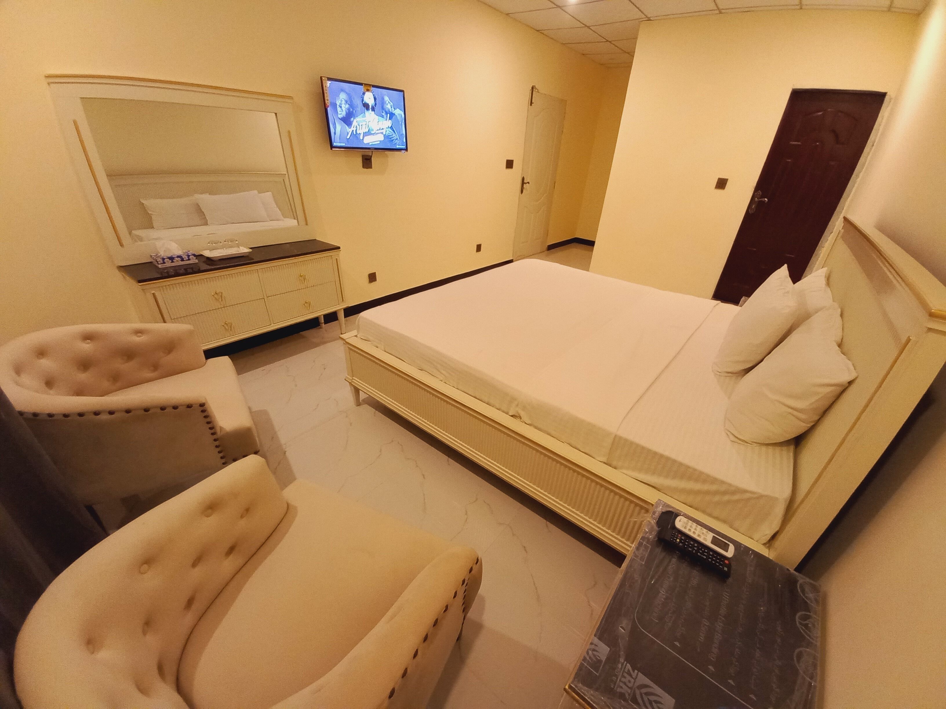 Quarto de hotel com uma cama, uma cadeira, uma cômoda, uma televisão e uma porta.