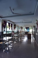 Um restaurante com várias mesas e cadeiras, ventiladores de teto e grandes janelas com cortinas.