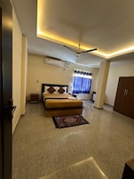 Quarto de hotel com cama, ventoinha no teto, ar condicionado, janela com cortinas e guarda-roupa de madeira.