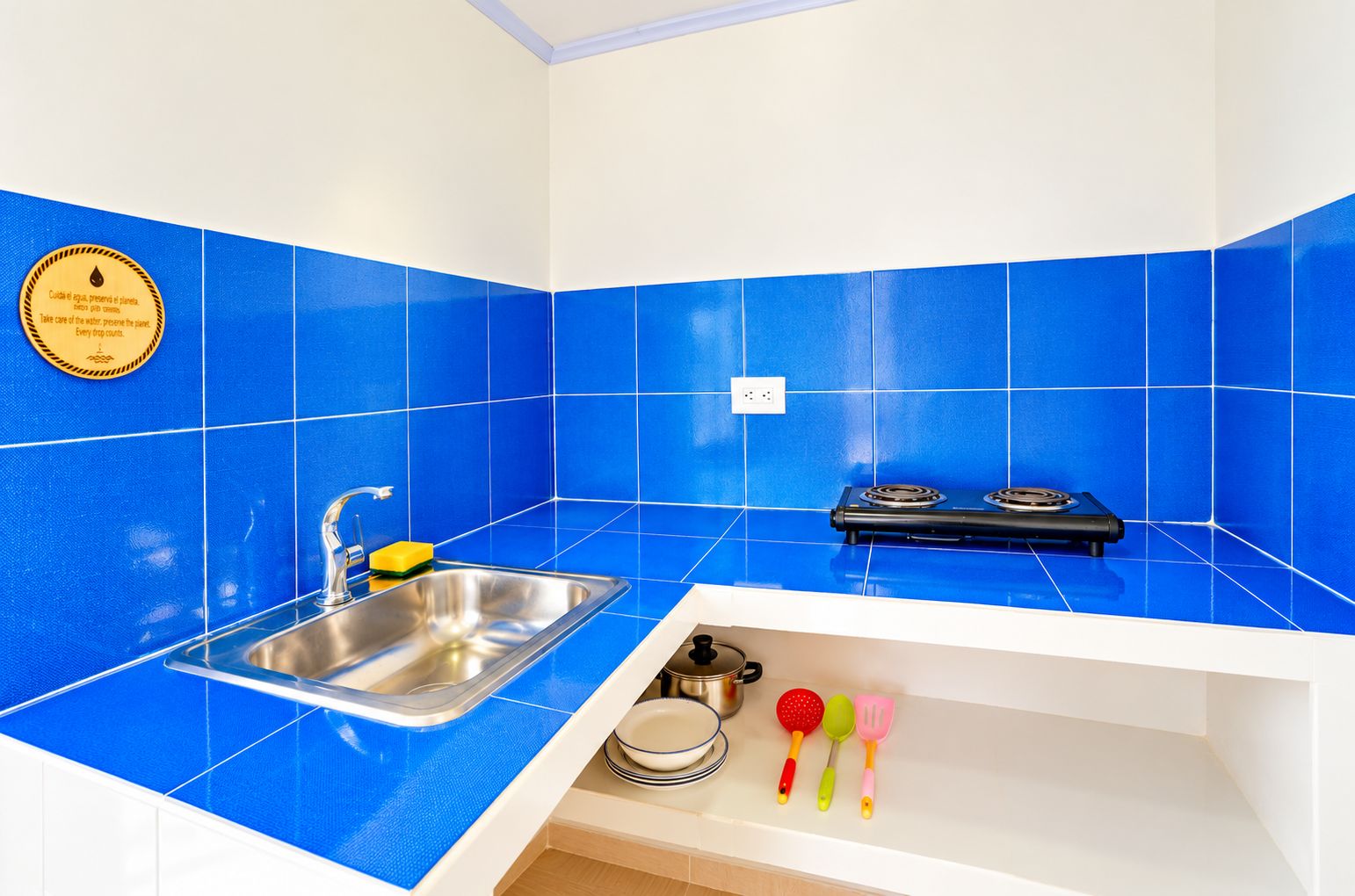 Cozinha com azulejos azuis, pia de aço inoxidável, fogão e escorredor de louça com pratos e utensílios.