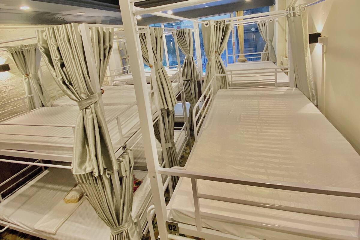 Um vagão de trem com várias beliches, cada uma com estrutura metálica branca e um colchão.