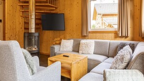 Interior acolhedor de uma cabana com decoração em madeira, lareira, sofá e televisão.