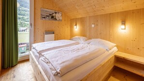 Quarto de cabana de madeira com duas camas, janela com cortinas, aquecedor fixado na parede e um quadro.