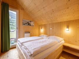 Quarto de cabana de madeira com duas camas, janela com cortinas, aquecedor fixado na parede e um quadro.