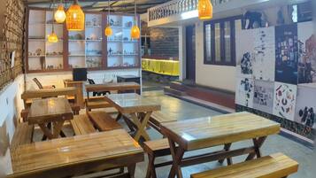 Interior de restaurante com mesas e bancos de madeira, luminárias pendentes laranja e uma parede decorada com diversos cartazes.