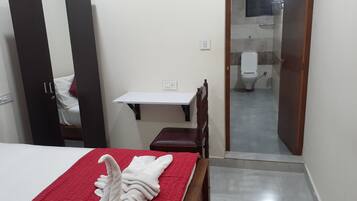 Quarto de hotel com uma cama, guarda-roupa de madeira, uma mesinha e um banheiro visível através de uma porta aberta.