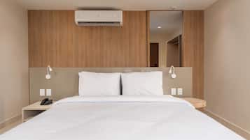 Quarto de hotel moderno com uma cama grande, painéis de madeira, ar condicionado embutido, abajures, um telefone na mesa de cabeceira e um espelho sobre a cama.