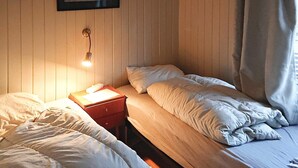 Uma cama de solteiro com roupa de cama branca, uma mesa de cabeceira com abajur e um quadro na parede.