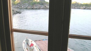 Vista pela janela de um pequeno barco atracado em um cais, com terreno rochoso ao fundo.