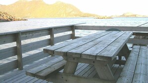 Uma mesa de piquenique de madeira em um píer, com vista para o mar e montanhas ao fundo.