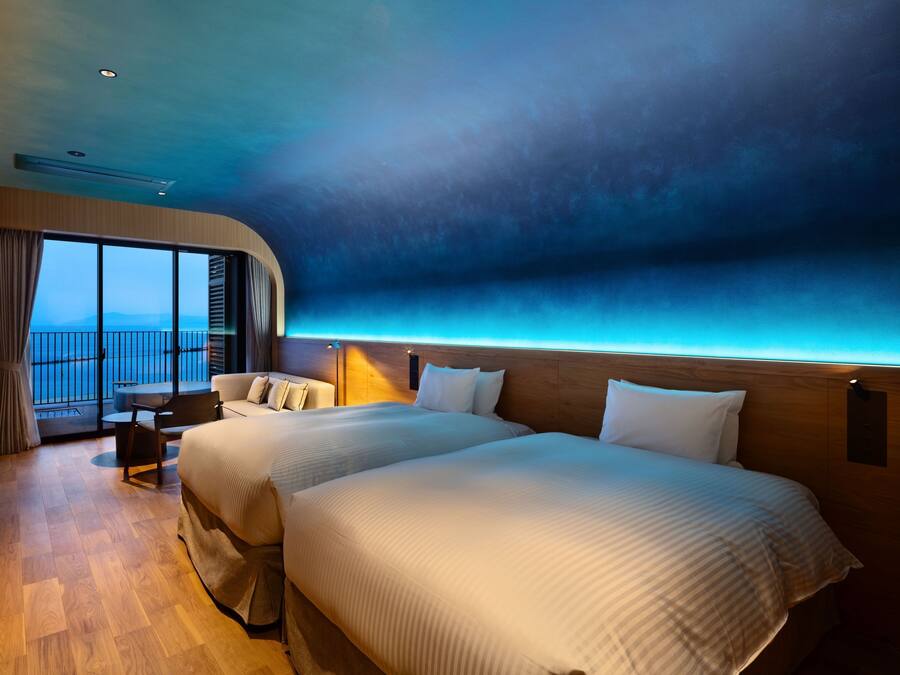 Quarto de hotel moderno com duas camas, varanda e vista para o mar, e piso de madeira.