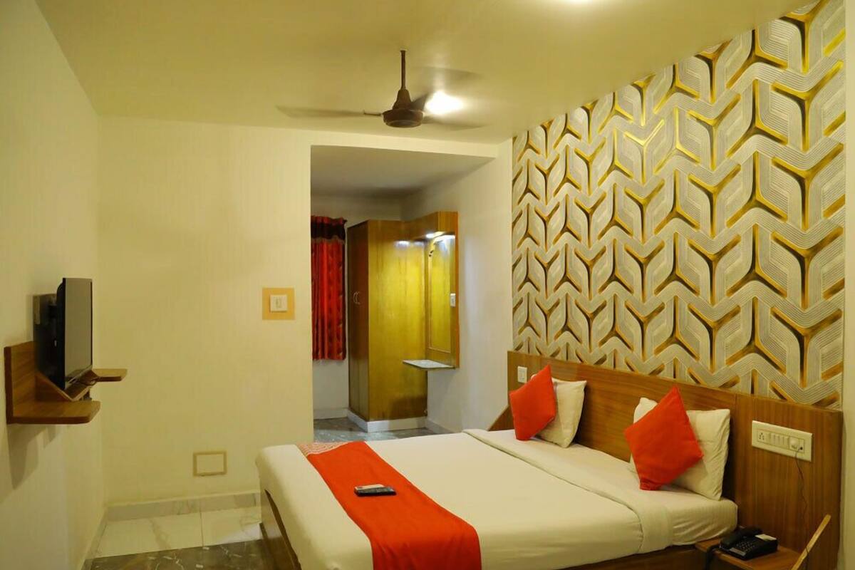 Quarto de hotel com cama, televisão em móvel, ventoinha no teto e parede estampada.