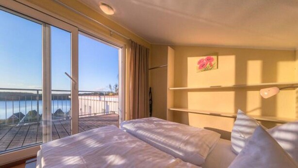 Quarto de hotel com duas camas, uma janela grande com vista para a água e um quadro na parede.
