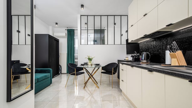 Uma cozinha moderna com bancada preta, armários brancos e uma área de refeições com mesa de vidro e cadeiras pretas.