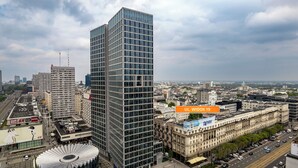 Um edifício alto com fachada de vidro moderna, rodeado por uma mistura de edifícios antigos e recentes em ambiente urbano.