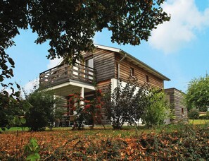 Uma casa de madeira de dois andares com uma varanda, rodeada por árvores e um jardim.