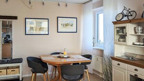 Uma área de refeições com mesa e cadeiras de madeira, uma luminária pequena e obras de arte emolduradas na parede.