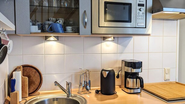 Cozinha moderna com pia de aço inoxidável, cafeteira, micro-ondas e máquina de lavar louça.