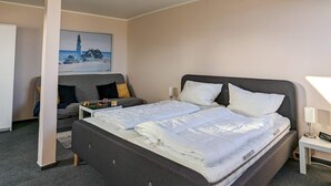 Quarto de hotel com uma cama grande, mesa de cabeceira, abajur e pintura de um farol na parede.