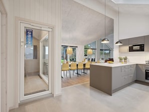 Cozinha moderna com ilha central, área de jantar com cadeiras amarelas e uma janela grande que ilumina com luz natural.