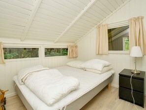 Quarto com cama, mesa de cabeceira, abajur e janela com cortinas.