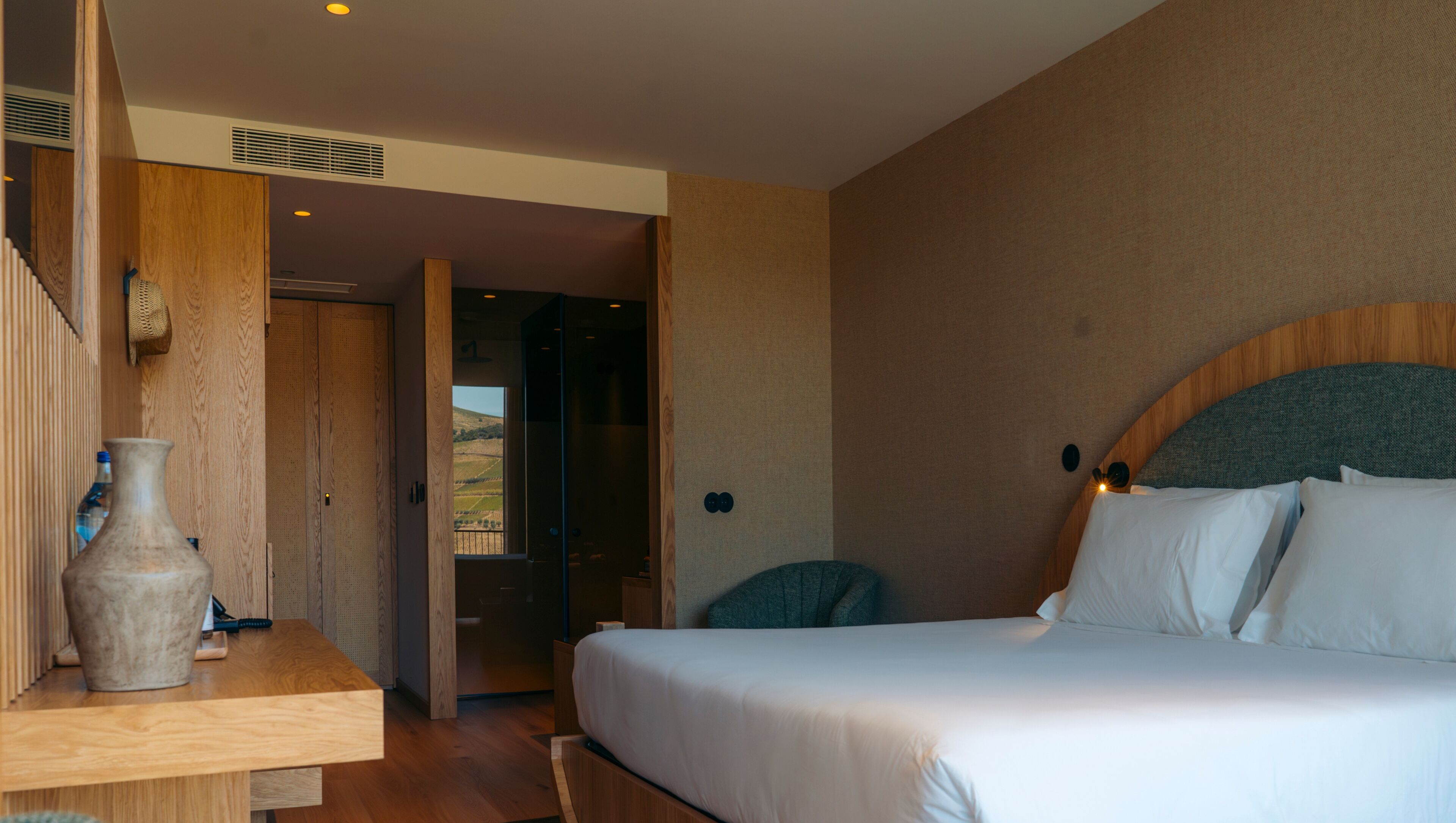 Quarto de hotel com uma cama, uma escrivaninha de madeira, um vaso e vista para o exterior.