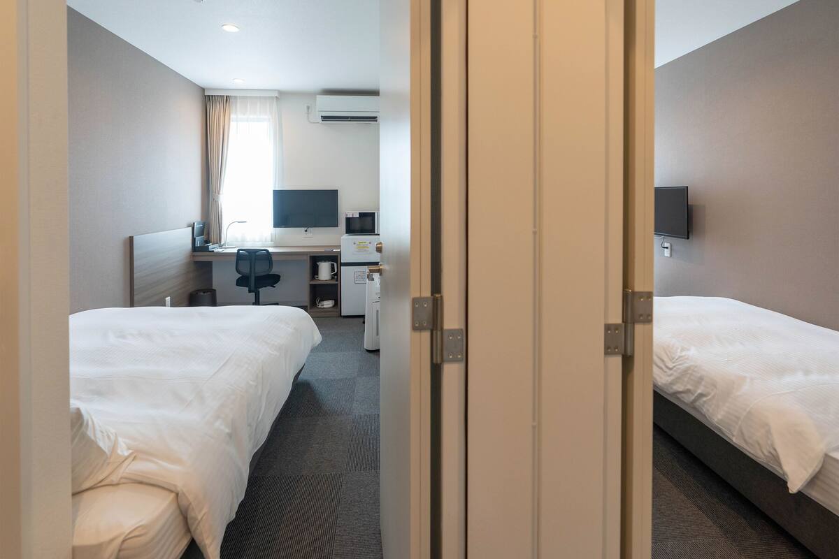 Quarto de hotel com duas camas, uma escrivaninha com computador, televisão e micro-ondas.