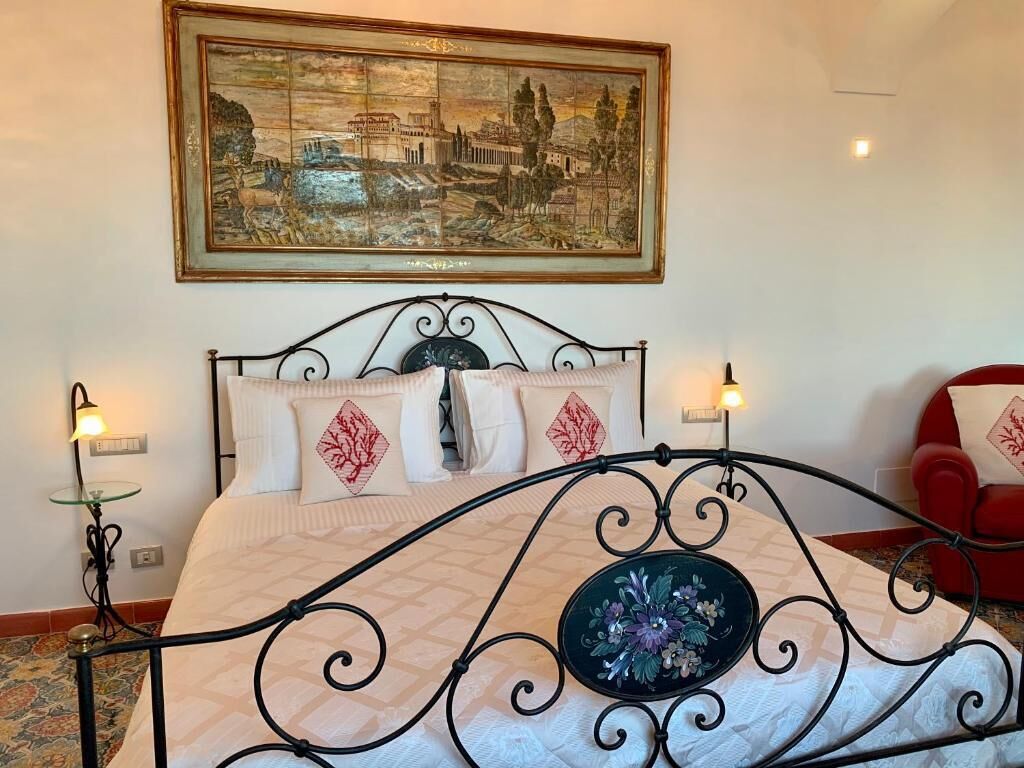Quarto bem arrumado com uma cama, duas luminárias laterais, uma cadeira vermelha e um quadro grande na parede.