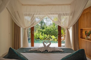 Uma cama com dossel, arranjo de toalhas em formato de coração e vista para uma piscina e vegetação.