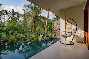 Uma área na beira da piscina com uma cadeira suspensa, cercada por vegetação tropical exuberante e uma parede de pedra.