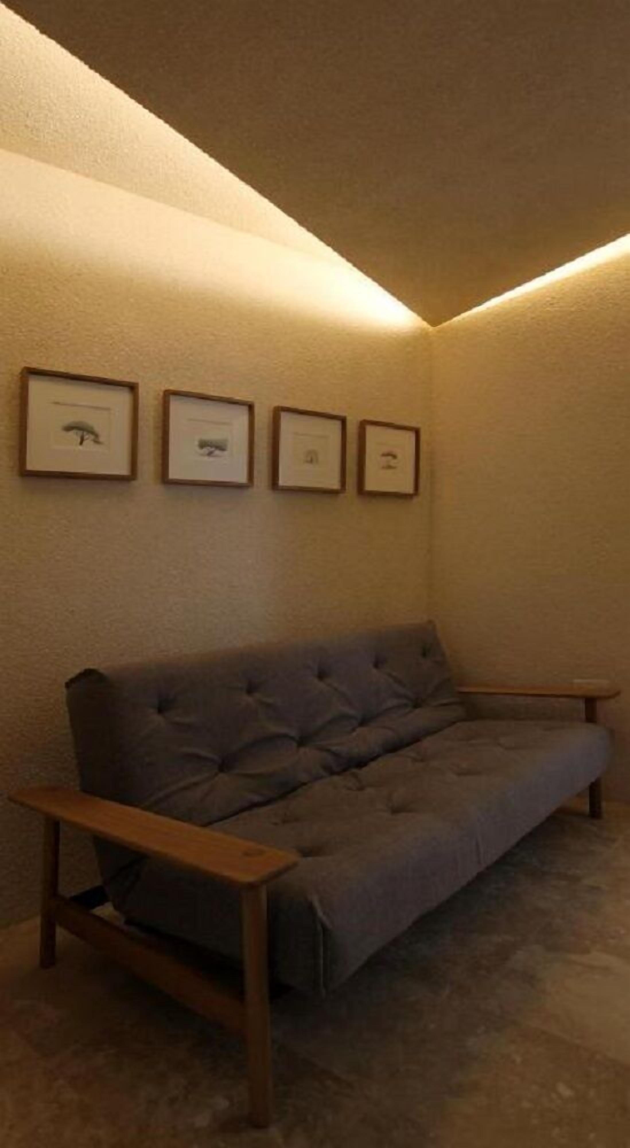 Um quarto aconchegante com um sofá cinza, uma mesa lateral de madeira e três quadros na parede.