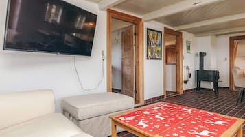 Uma sala de estar acolhedora com televisão de tela plana na parede, um sofá, uma mesa de centro de madeira com jogos americanos vermelhos e uma lareira a lenha.