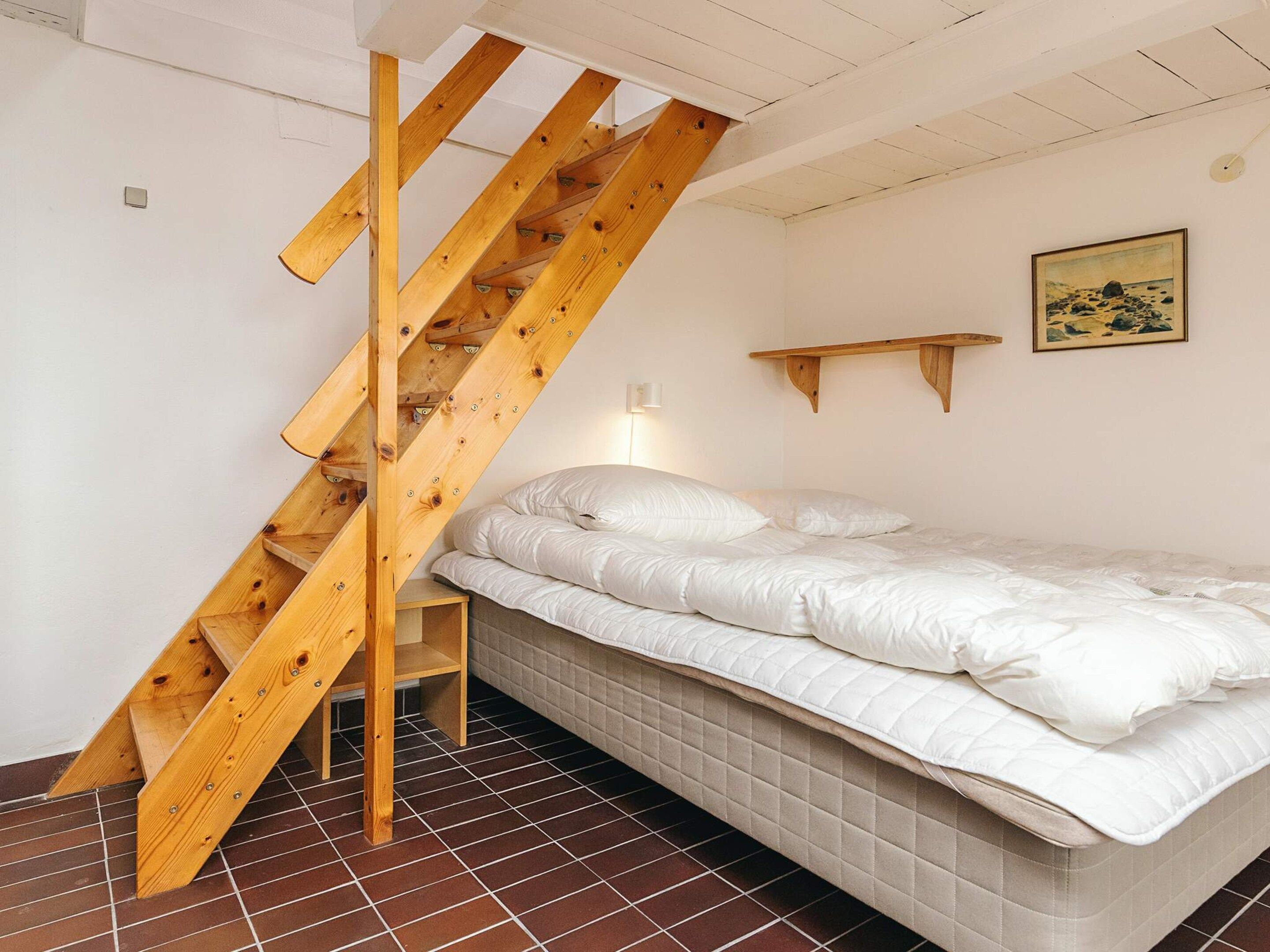 Quarto com escada de madeira, cama com roupa de cama branca, piso ladrilhado e prateleira fixada na parede.