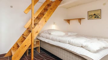 Quarto com escada de madeira, cama com roupa de cama branca, piso ladrilhado e prateleira fixada na parede.