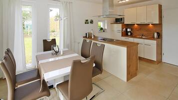 Uma cozinha moderna com armários brancos, uma ilha central e um espaço de jantar com mesa e cadeiras.