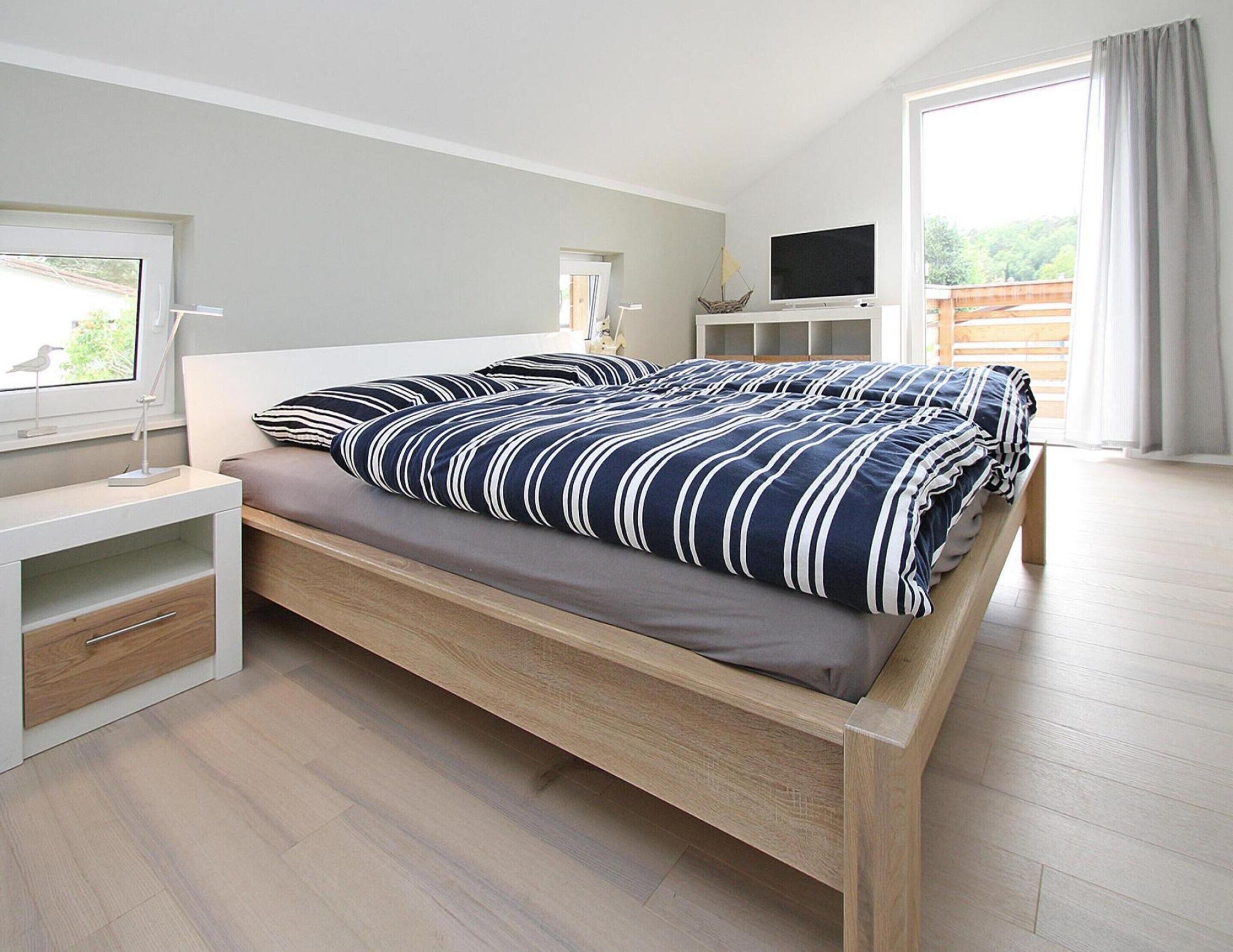 Quarto moderno com cama de madeira, mesa de cabeceira com abajur e televisão em móvel.