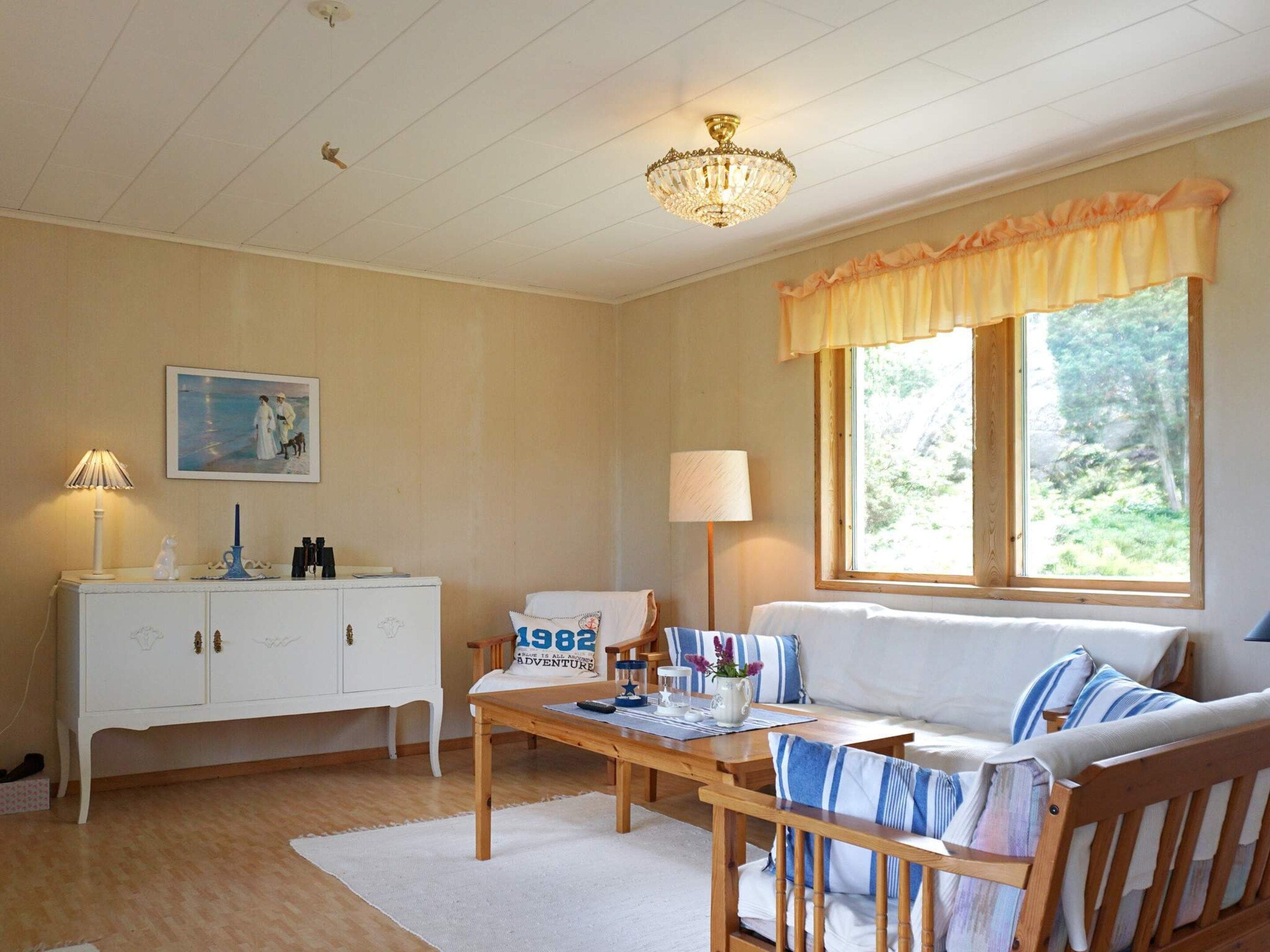 Uma sala de estar aconchegante com sofá, mesa de centro de madeira, armário branco, lustre e janela com cortinas.
