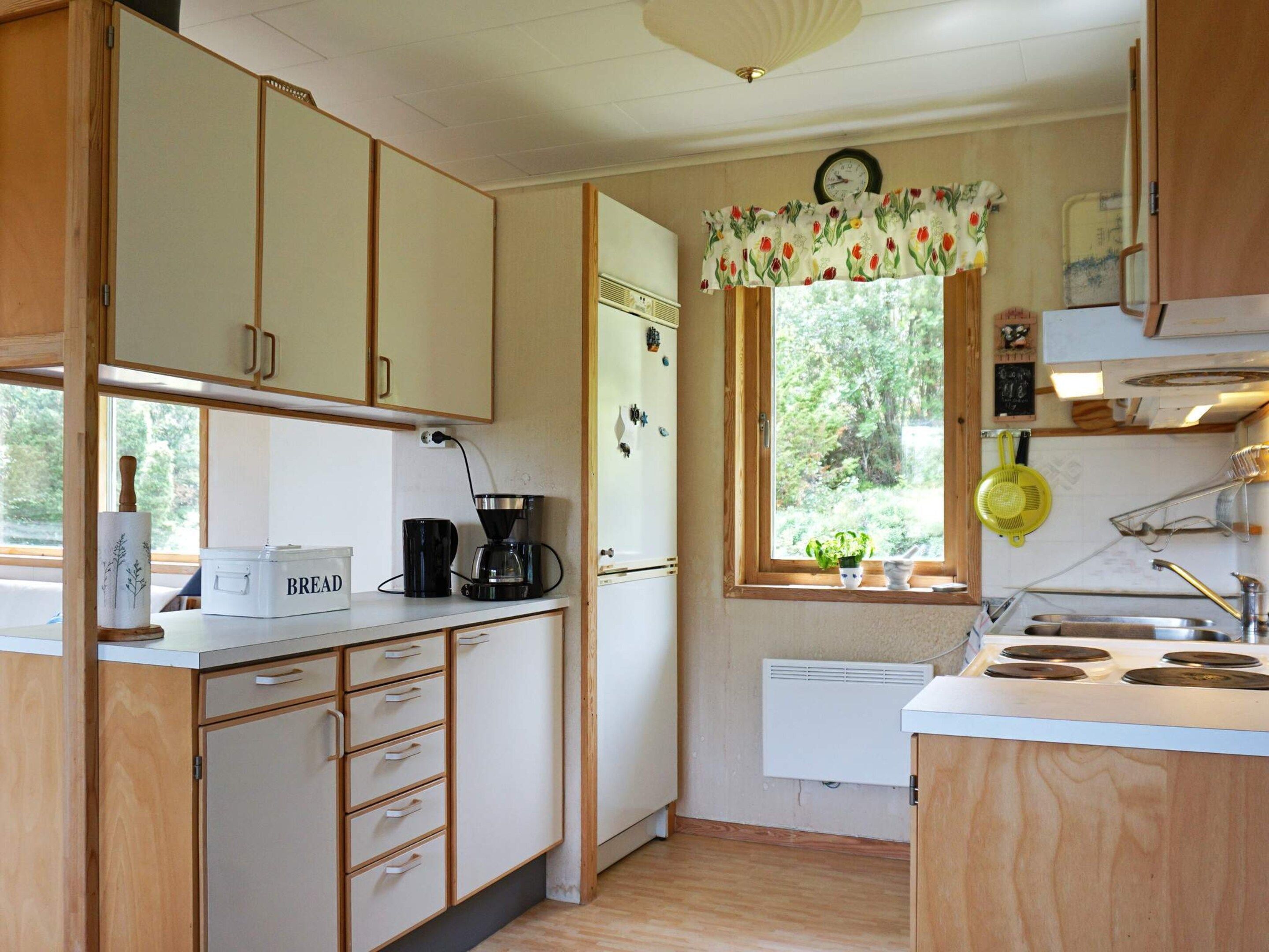 Cozinha compacta com armários de madeira, cafeteira, geladeira e janela com vista para o verde.