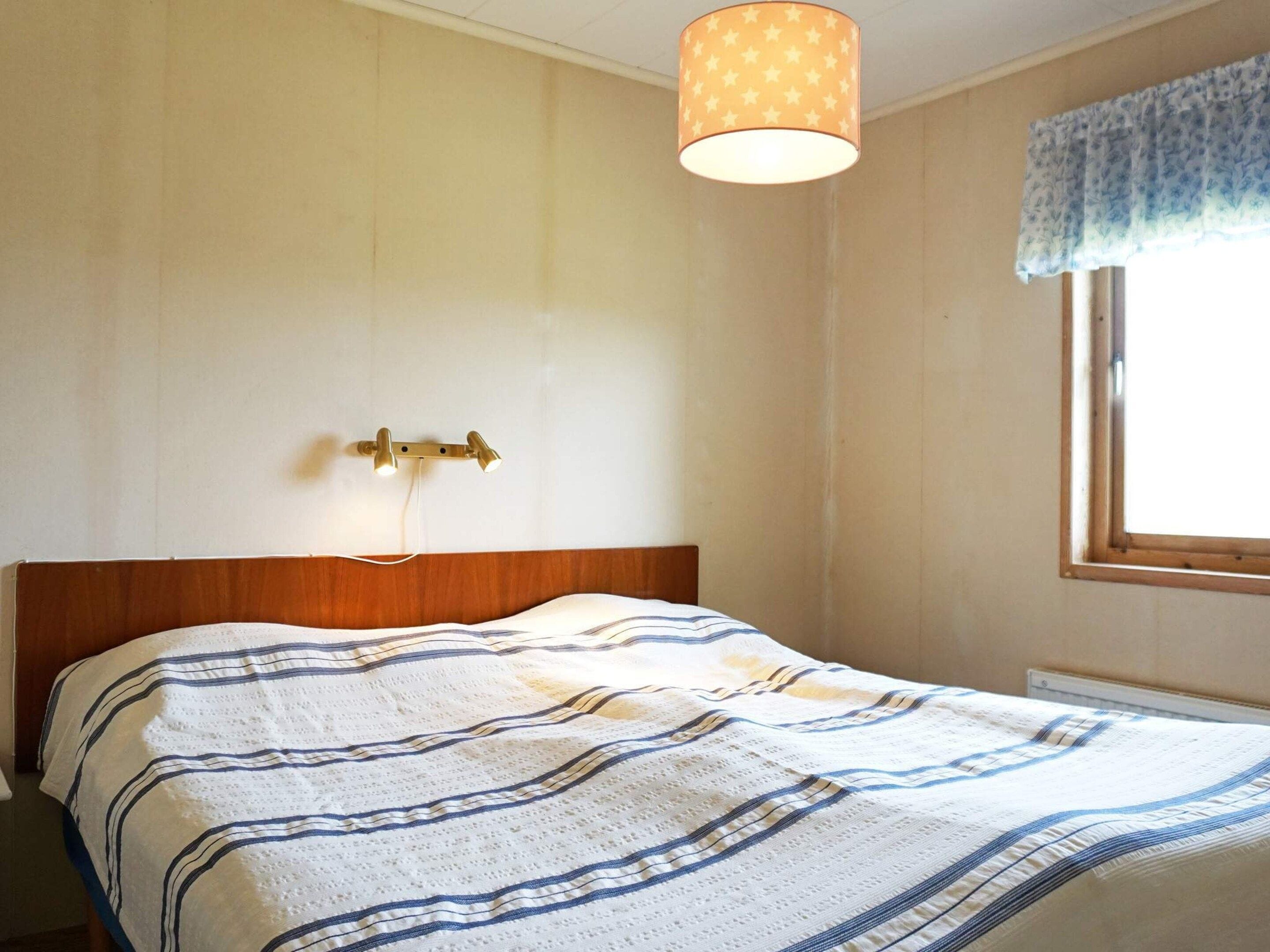 Quarto com cama, luminária na parede e janela com cortina.